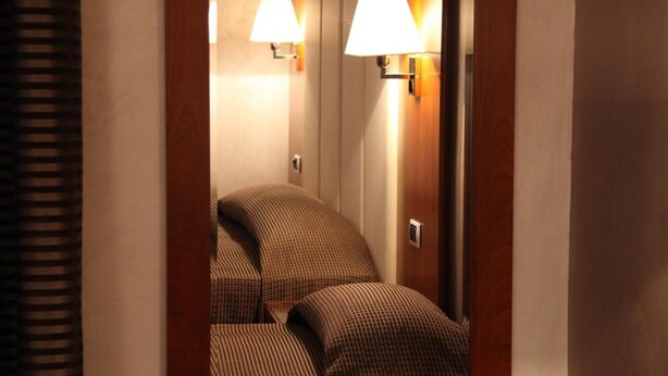 Quarto de hotel com um espelho grande, duas luminárias de cabeceira e uma cama com roupa de cama estampada.