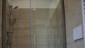 Uma casa de banho moderna com cabine de duche em vidro, sanita branca e painel de controlo fixado à parede.