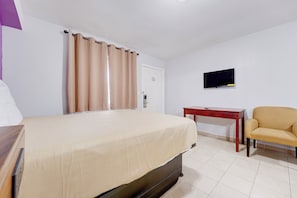 Quarto de hotel com cama, escrivaninha, cadeira, televisão e porta.
