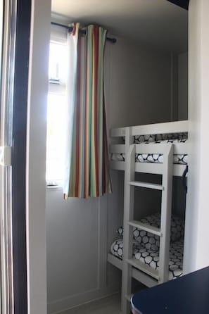 Uma cama de solteiro com roupa de cama estampada, uma cortina listrada e vista para uma janela.