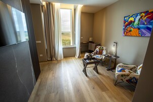 Uma sala de estar moderna com uma janela grande, uma televisão de tela plana, um sofá, uma mesinha com abajur e um quadro colorido na parede.