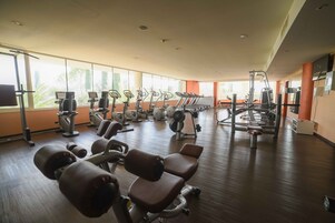 Uma academia espaçosa com máquinas de cardio, estações de musculação e uma grande janela que oferece iluminação natural.