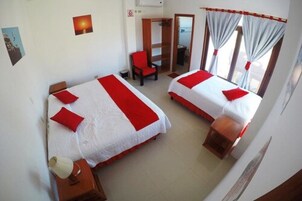 Quarto de hotel com duas camas, cada uma com roupa de cama vermelha e branca, uma pequena cadeira de madeira, um espelho e uma janela com cortinas.