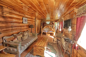 Interior de uma cabana de madeira com sofá, poltrona e mesa de centro em madeira.
