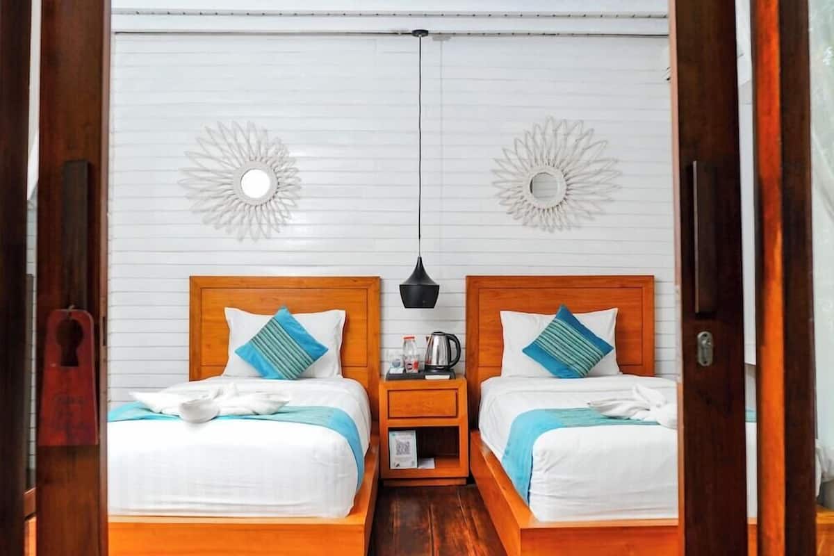 Quarto duplo com duas camas, cabeceiras de madeira, mesa de cabeceira com abajur e girassóis decorativos na parede.