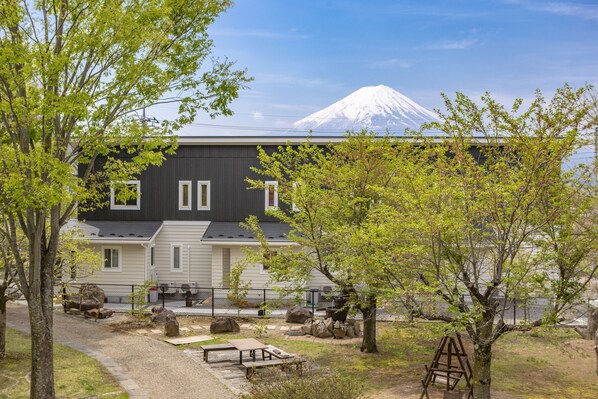 Uma casa moderna com vista para uma montanha nevada, cercada por árvores e um pátio com mobiliário de exterior.