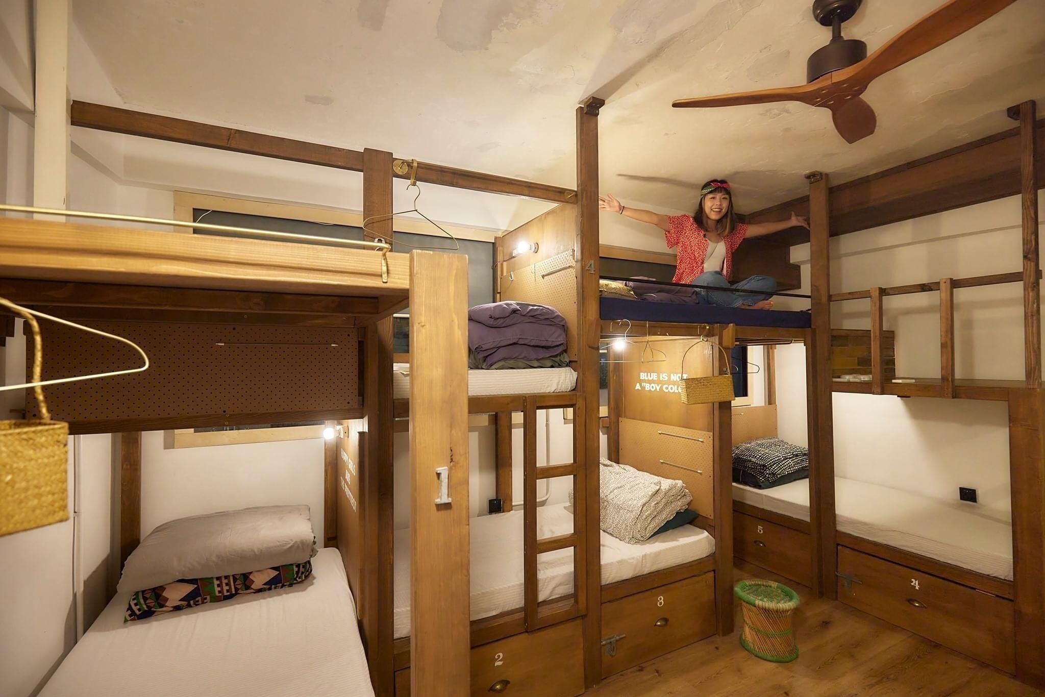 Quarto compacto com beliches, mobiliário de madeira e ventoinha.