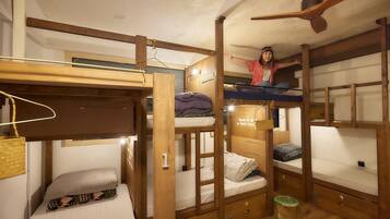 Quarto compacto com beliches, mobiliário de madeira e ventoinha.