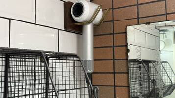 Um ar condicionado fixado na parede com grelha metálica, parede revestida com azulejos em tons de branco e castanho, e guarda-corpo de metal.