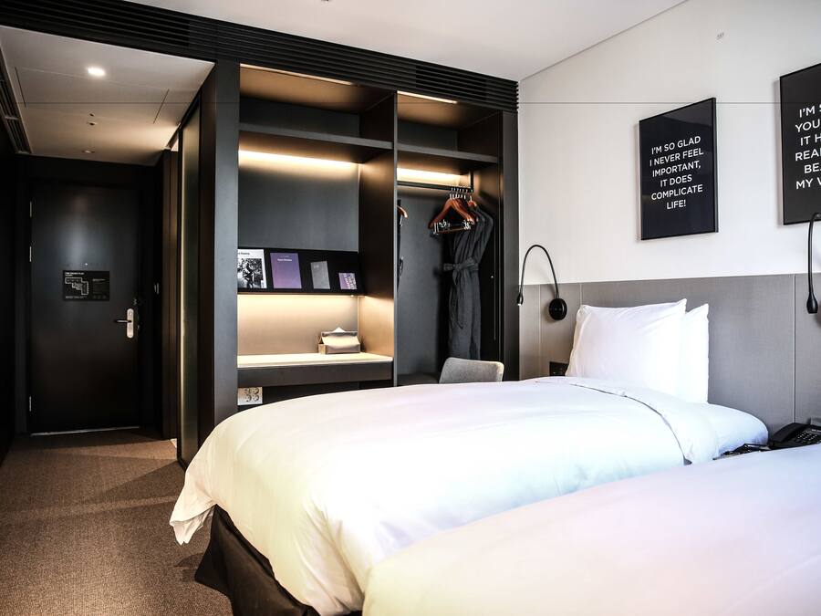 Quarto de hotel com uma cama grande, uma mesa de escritório e um guarda-roupa. Há citações motivacionais na parede.