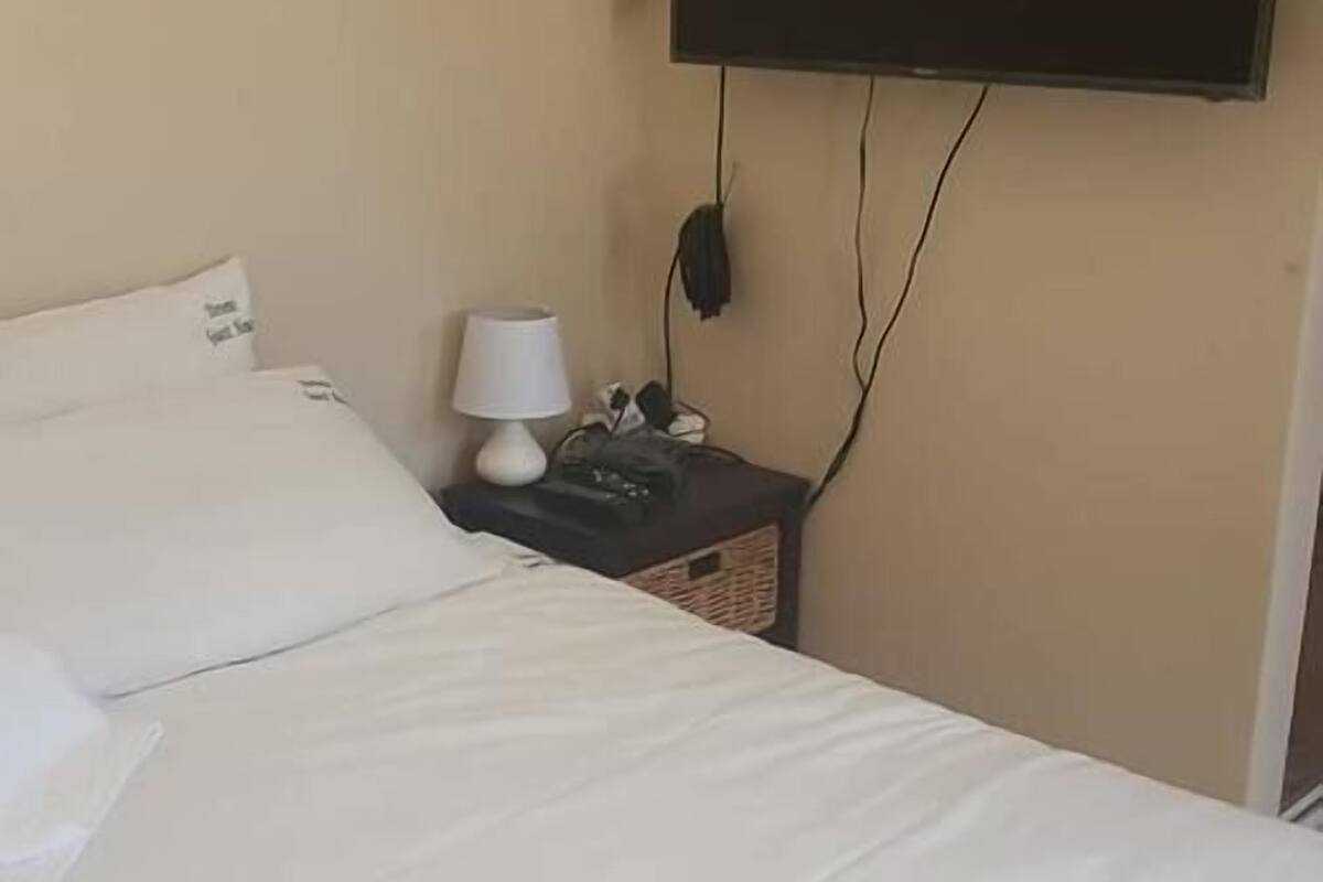 Quarto de hotel com uma cama, uma mesa de cabeceira com abajur e uma televisão fixada na parede.