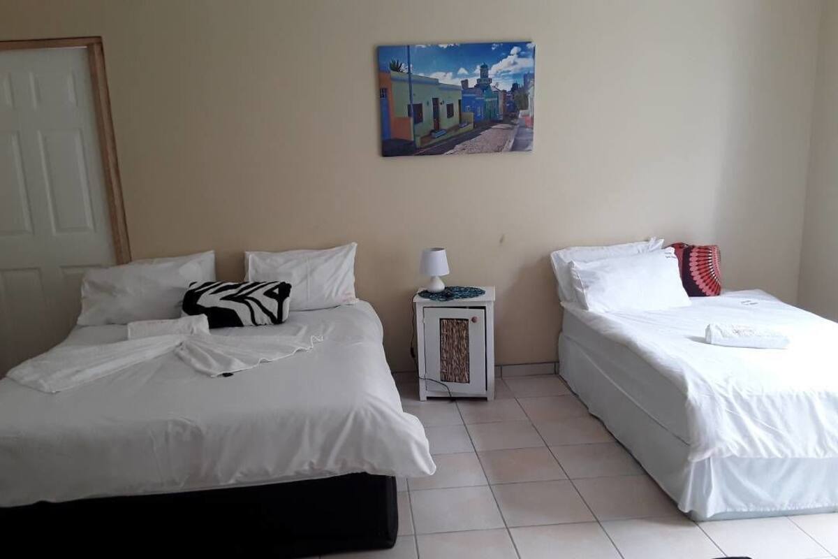 Quarto de hotel com duas camas, uma mesinha com abajur e um quadro na parede.