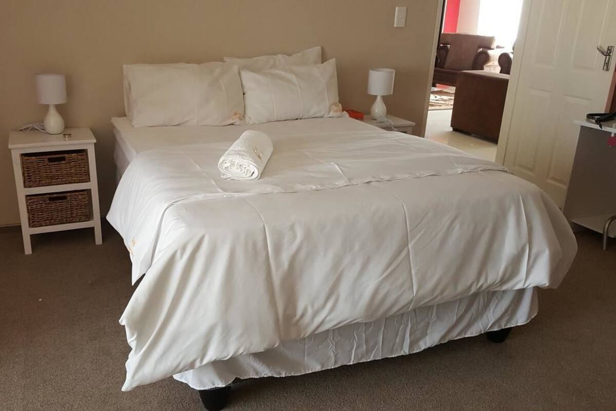 Cama bem arrumada com uma toalha enrolada, duas mesas de cabeceira com abajures e uma pequena cesta de vime em uma das mesas.