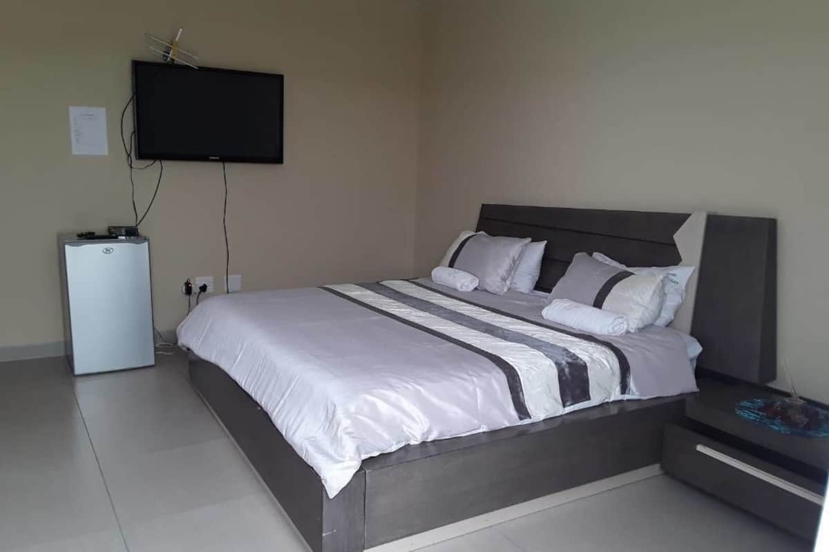 Quarto com cama, televisão na parede, pequena escrivaninha e uma cadeira.
