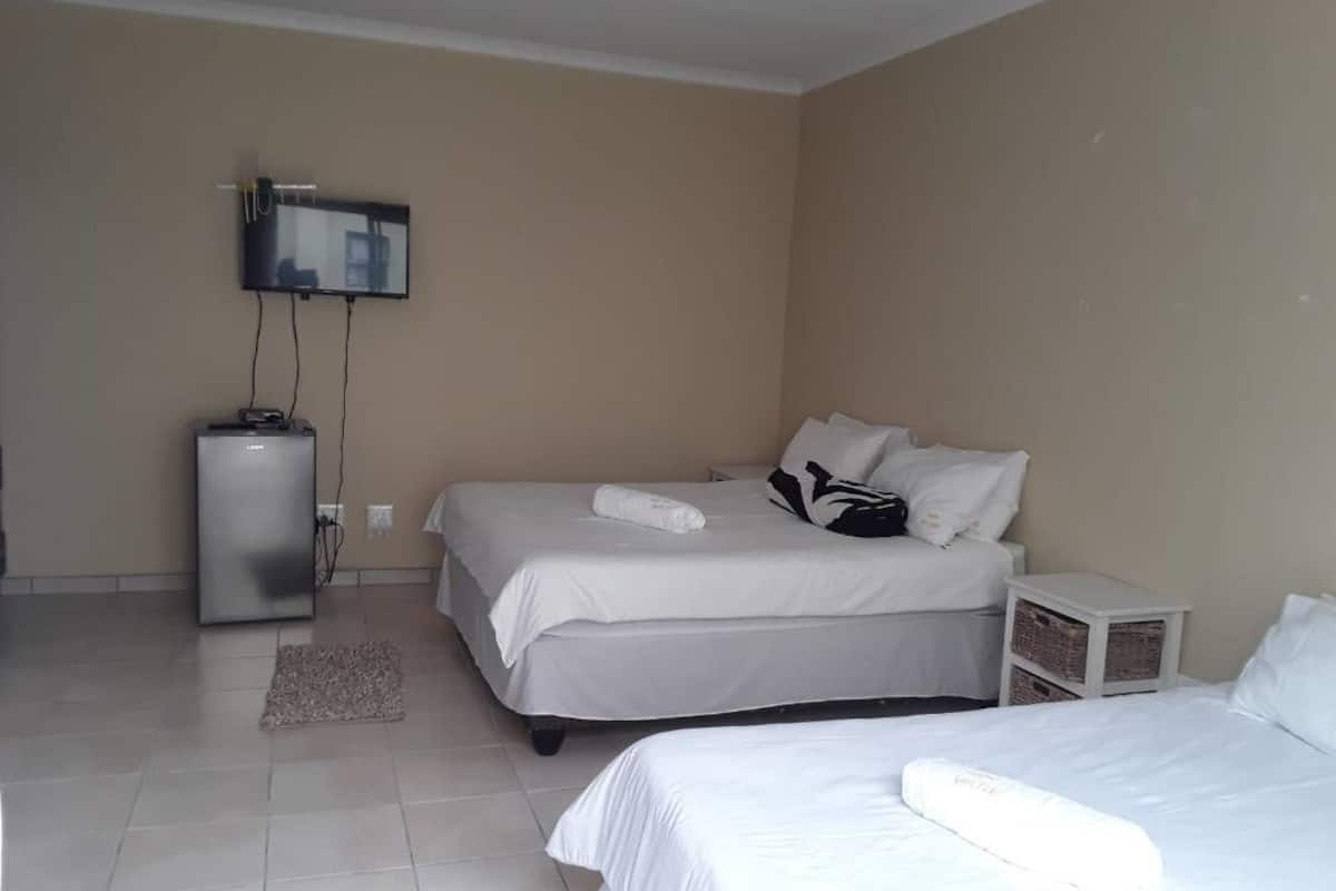 Quarto de hotel com duas camas, televisão, minibar e uma pequena mesa de cabeceira branca.