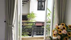 Varanda aberta com vista para um edifício, planta em vaso e um vaso de girassóis.