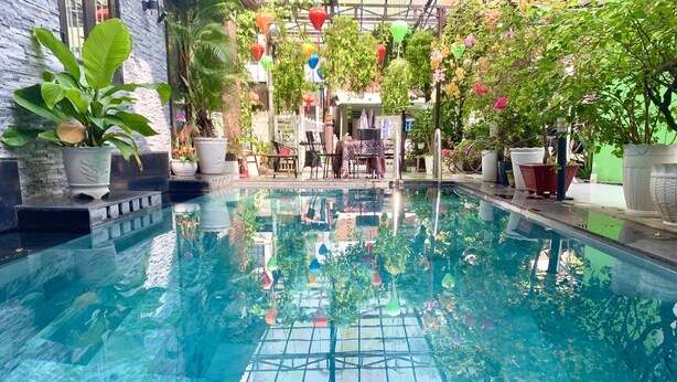 Piscina interna com água cristalina, rodeada por plantas em vasos e decorações penduradas.