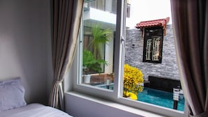 Quarto com uma janela grande, uma cama e vista para uma piscina e um edifício com telhado vermelho.