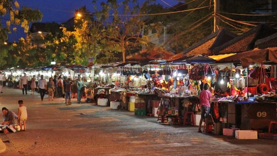 Mercado noturno ao ar livre com diversos pontos de venda oferecendo produtos, iluminado por luminárias de rua.