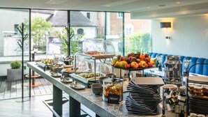 Disposição de buffet com diversos alimentos e acompanhamentos, um canto para café e uma área de estar com vista para o exterior.