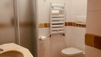 Casa de banho com sanita, chuveiro e suporte para toalhas.