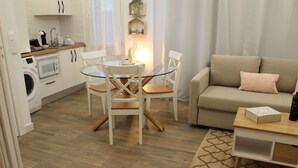 Um espaço compacto com cozinha compacta, área de refeições com mesa de vidro e sofá com almofada decorativa.