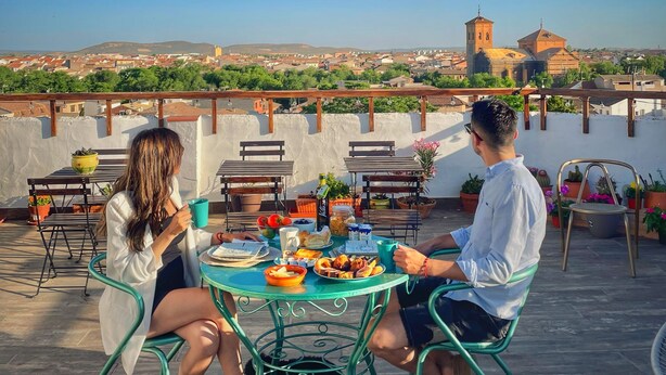 Terraço no telhado com uma mesa posta para dois, com diversos pratos e bebidas.