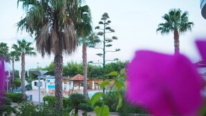 Um resort com palmeiras, piscina e um edifício com telhado de azulejos.