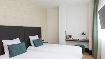 Quarto de hotel com duas camas, uma escrivaninha, uma cadeira e uma televisão.