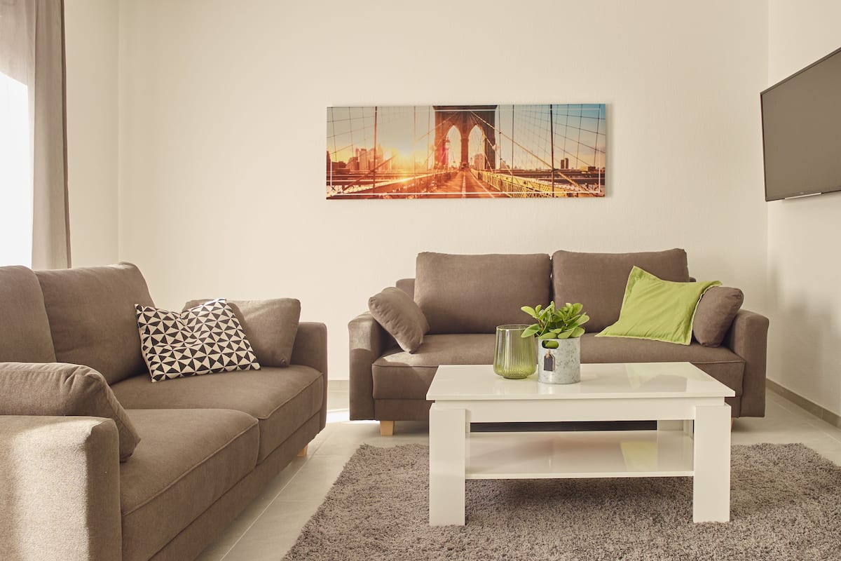Uma sala de estar com dois sofás, uma mesa de centro e um quadro de uma ponte.