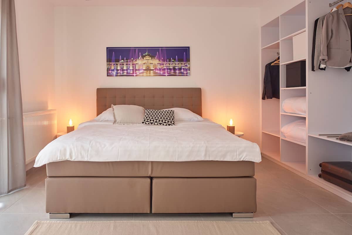 Quarto com cama grande, cabeceira, mesas de cabeceira com abajures, guarda-roupa e um quadro na parede.