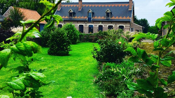 Uma casa grande e tradicional com telhado de telhas, rodeada por um jardim bem cuidado e um céu claro.