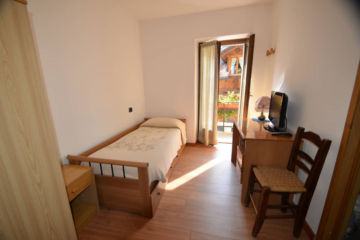 Quarto com cama de madeira, uma escrivaninha com cadeira e vista para uma varanda.