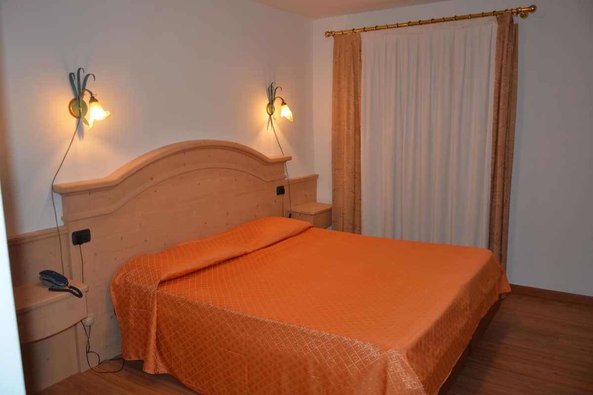 Uma cama de solteiro com colcha laranja em quarto com cabeceira de madeira e duas luminárias fixadas na parede.