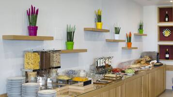 Uma área de buffet com diversos alimentos e utensílios, incluindo tigelas de cereais, frutas e uma seleção de bebidas.