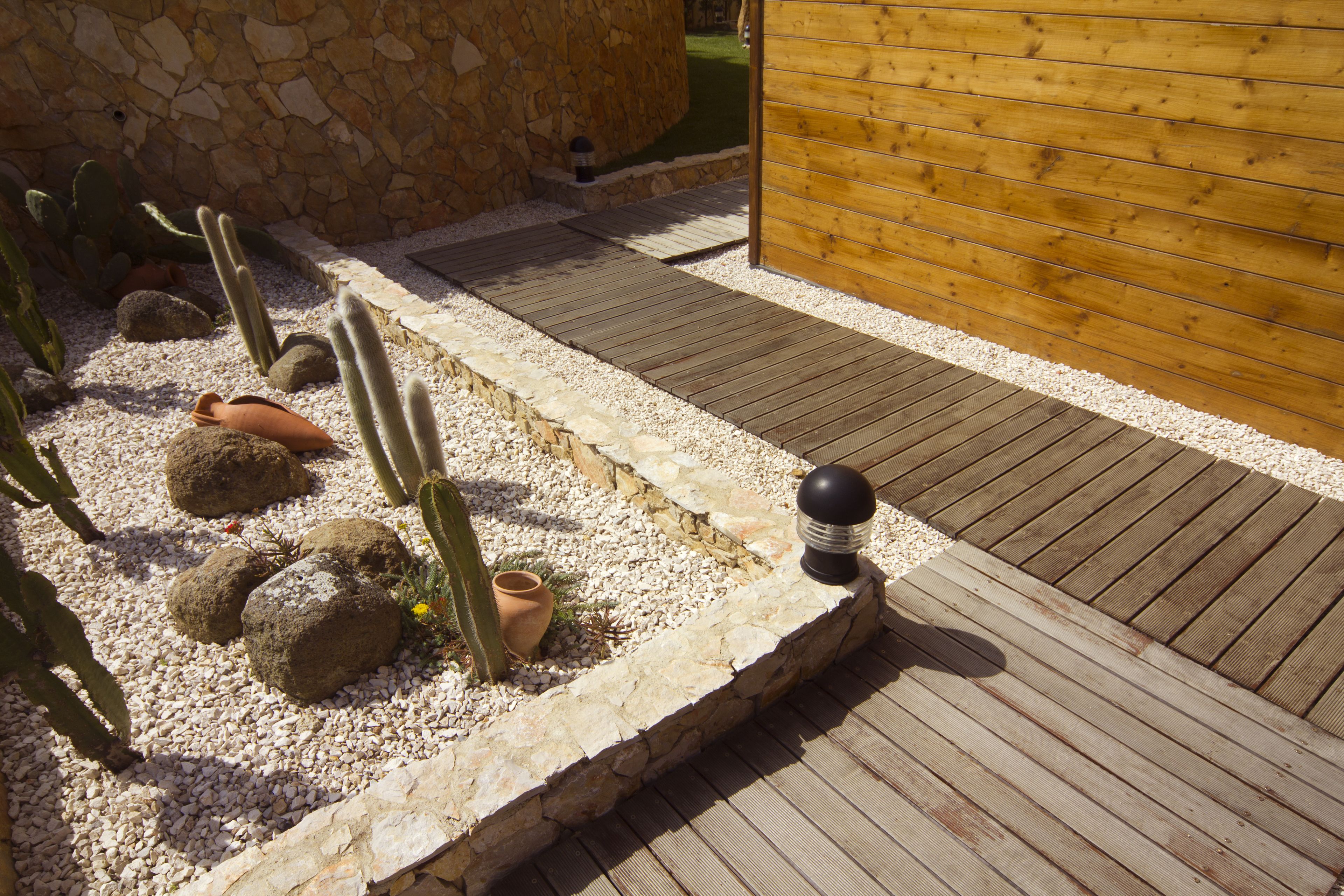 Um jardim com cactos e pedras, deck de madeira e um muro de pedra.