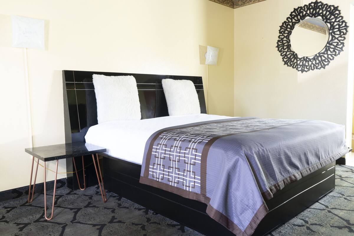 Cama bem arrumada com colcha estampada, mesa de cabeceira e espelho fixado na parede.
