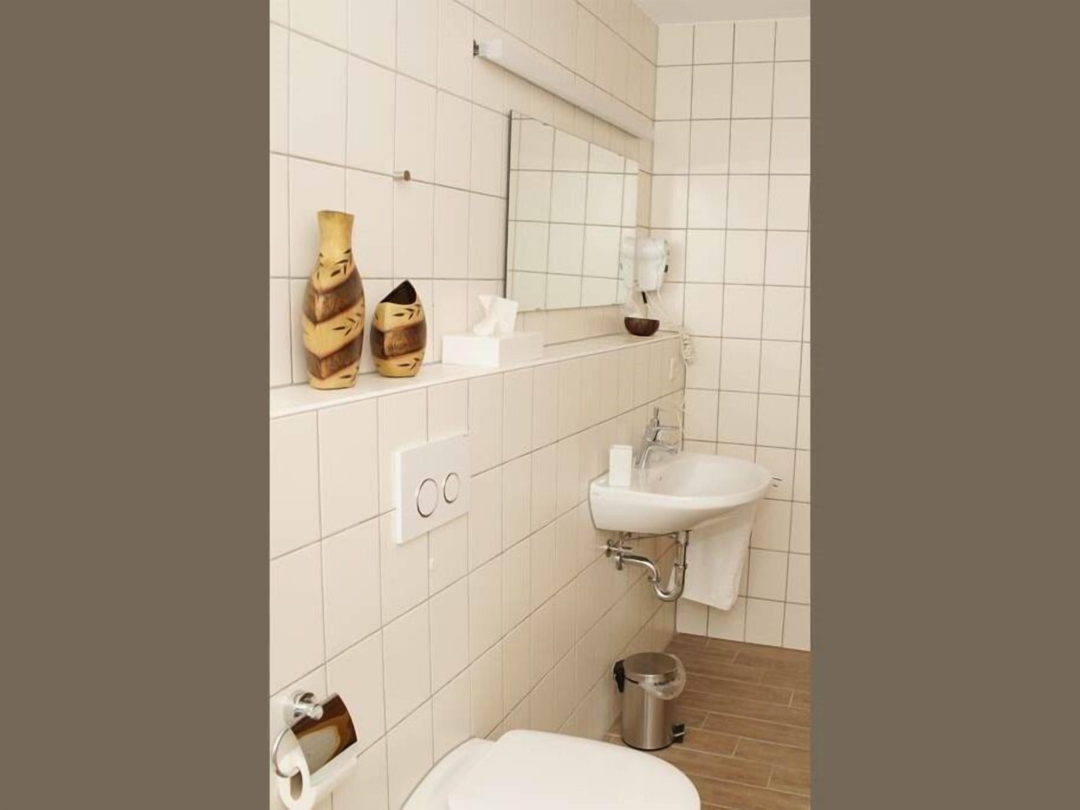 Um banheiro com pia branca, espelho e vaso sanitário. Há dois vasos decorativos na parede acima da pia.