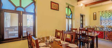Uma sala de jantar com mesas e cadeiras de madeira, um buffet montado e painéis de janela decorativos.