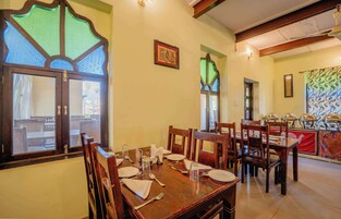Uma sala de jantar com mesas e cadeiras de madeira, um buffet montado e painéis de janela decorativos.
