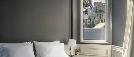 Quarto de hotel com uma cama grande, uma mesa de cabeceira, uma luminária e uma janela com vista para um edifício histórico.