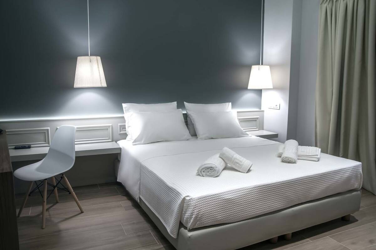 Quarto de hotel moderno com uma cama grande, duas luminárias de cabeceira, uma mesa e uma cadeira.
