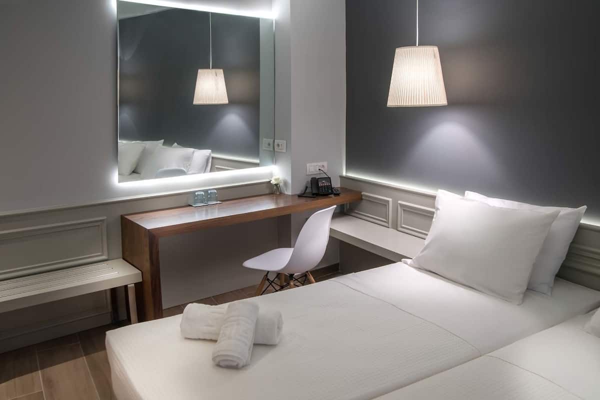 Quarto de hotel moderno com uma cama grande, uma escrivaninha, uma cadeira e um espelho amplo.