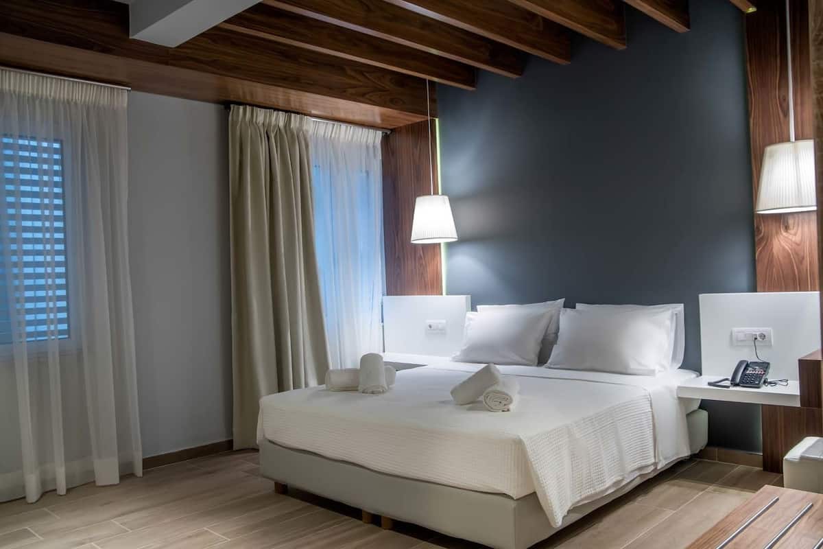 Quarto de hotel moderno com uma cama grande, duas mesas de cabeceira, uma escrivaninha e uma janela com cortinas.