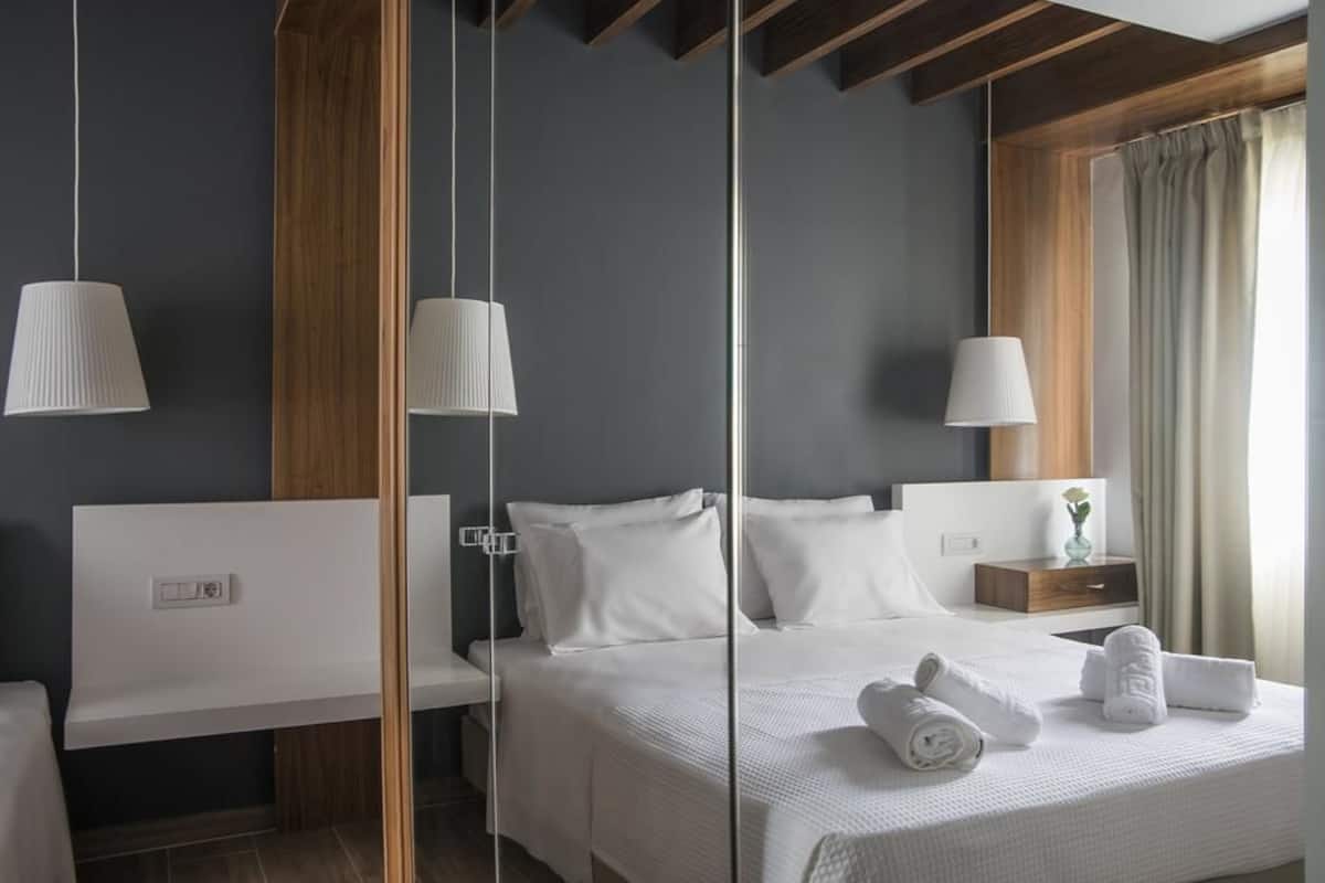 Quarto de hotel moderno com uma cama grande, mesas de cabeceira e um espelho.