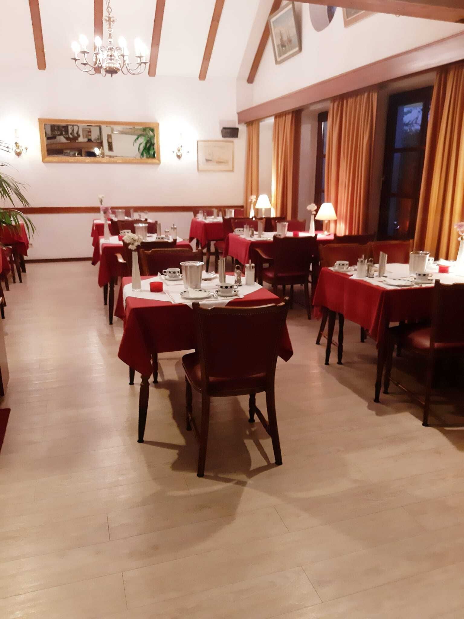 Restaurante com várias mesas preparadas para refeições, vigas de madeira no teto e um candelabro.