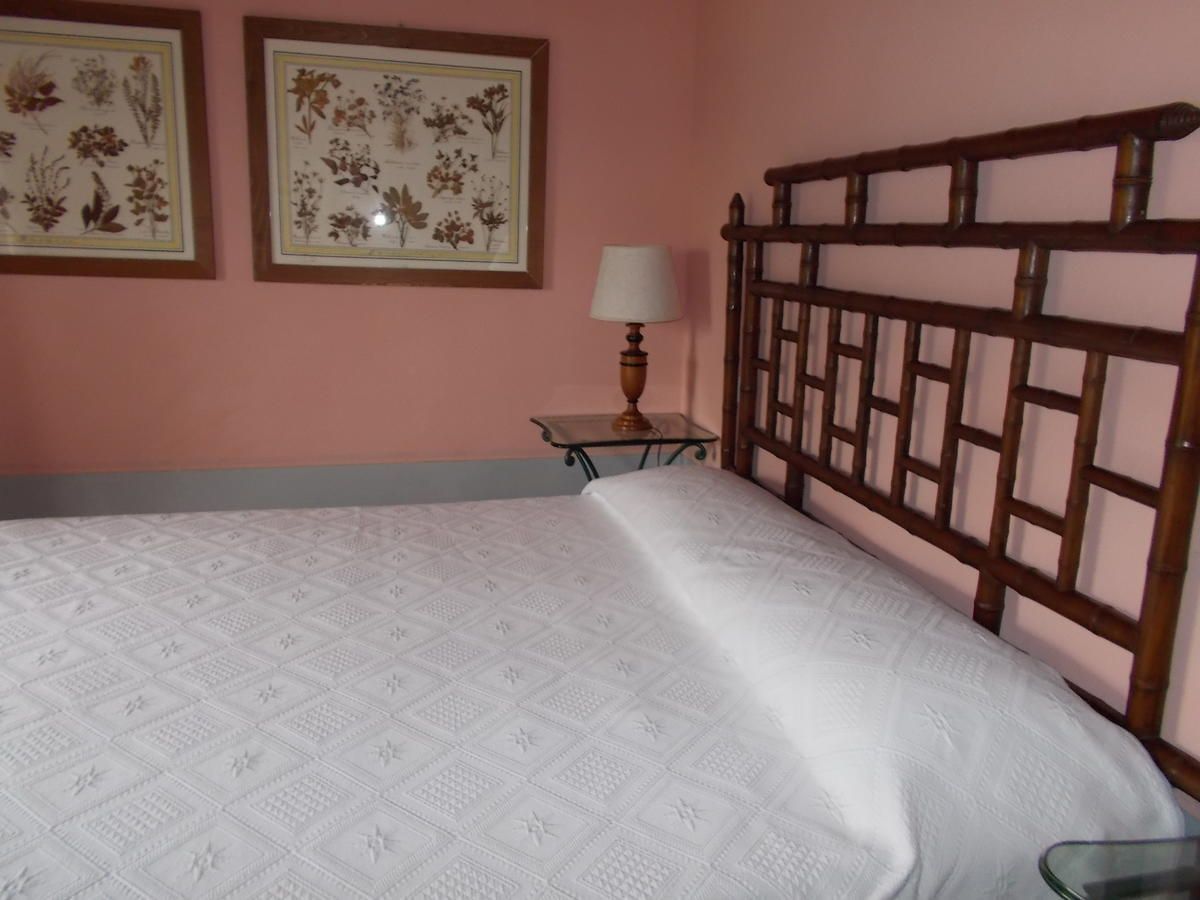 Quarto com cabeceira de madeira, cama com colcha branca e duas gravuras botânicas emolduradas na parede.
