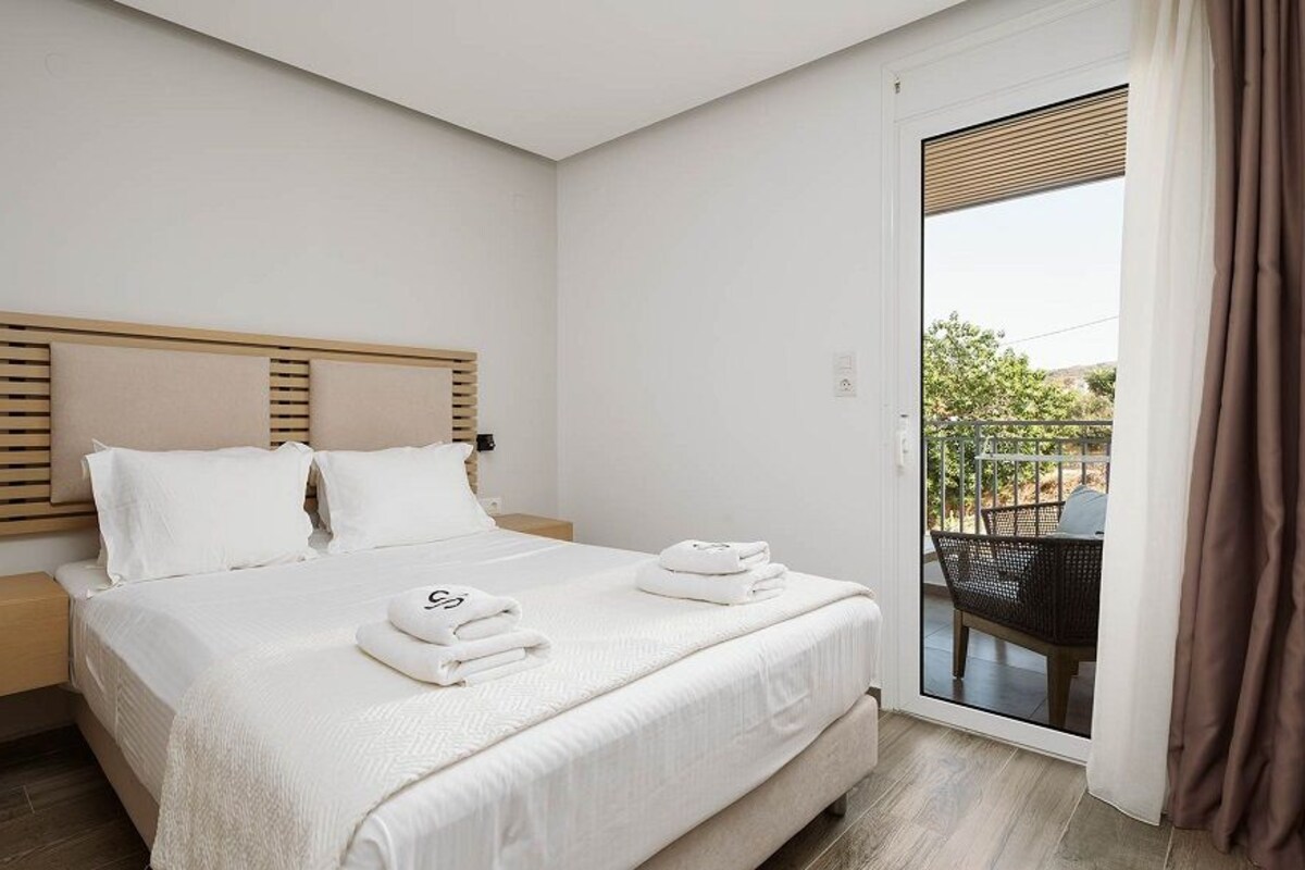 Quarto de hotel com cama, mesa de cabeceira, janela com vista e porta.