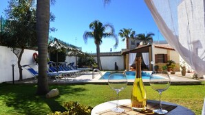Uma área à beira da piscina com uma mesa, dois copos de vinho e uma garrafa.