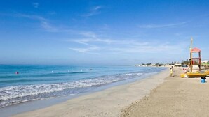 Uma praia com uma torre salva-vidas, céu azul claro e mar calmo.